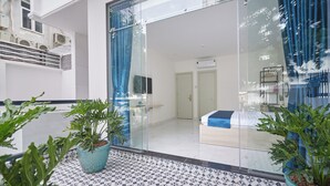 Quarto de hotel moderno com porta de vidro, cama com manta azul e um vaso de planta.