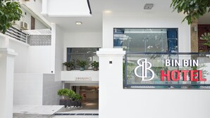 Entrada de hotel com balcão de recepção, plantas em vasos e vista clara do interior.