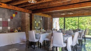 Uma área de refeições com parede de tijolos, uma mesa comprida com cadeiras e vista para o verde lá fora.