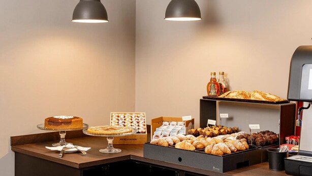Um buffet de café da manhã com diversos pães, uma máquina de café e uma seleção de acompanhamentos.