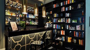 Uma área de bar com balcão, prateleiras cheias de garrafas de bebidas e luminárias pendentes.