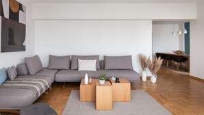 Uma sala de estar moderna com um sofá seccional cinza, uma mesa de centro de madeira e uma área de jantar com mesa e cadeiras de madeira.