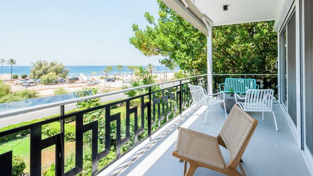 Uma varanda com vista para a praia, cadeiras brancas e uma mesa.