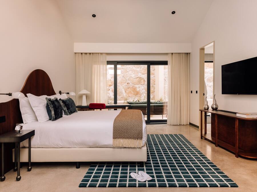 Quarto de hotel moderno com uma cama grande, televisão de tela plana, uma mesa pequena e vista para o exterior através de uma janela ampla.