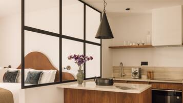 Cozinha moderna com ilha central, banquetas pretas, luminária pendente e cabeceira de madeira no quarto vizinho.