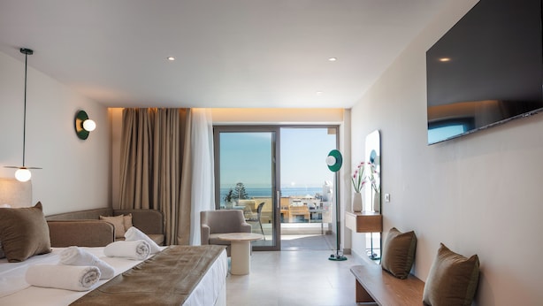 Quarto de hotel moderno com uma cama, um sofá, uma mesa redonda e uma TV fixada na parede.