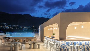Um bar no terraço com vista para a piscina, banquetas e mesas ao ar livre.