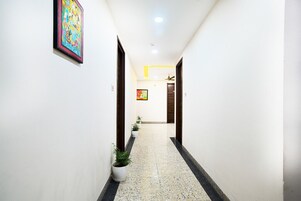 Um corredor com paredes brancas, detalhes em preto e plantas em vasos.