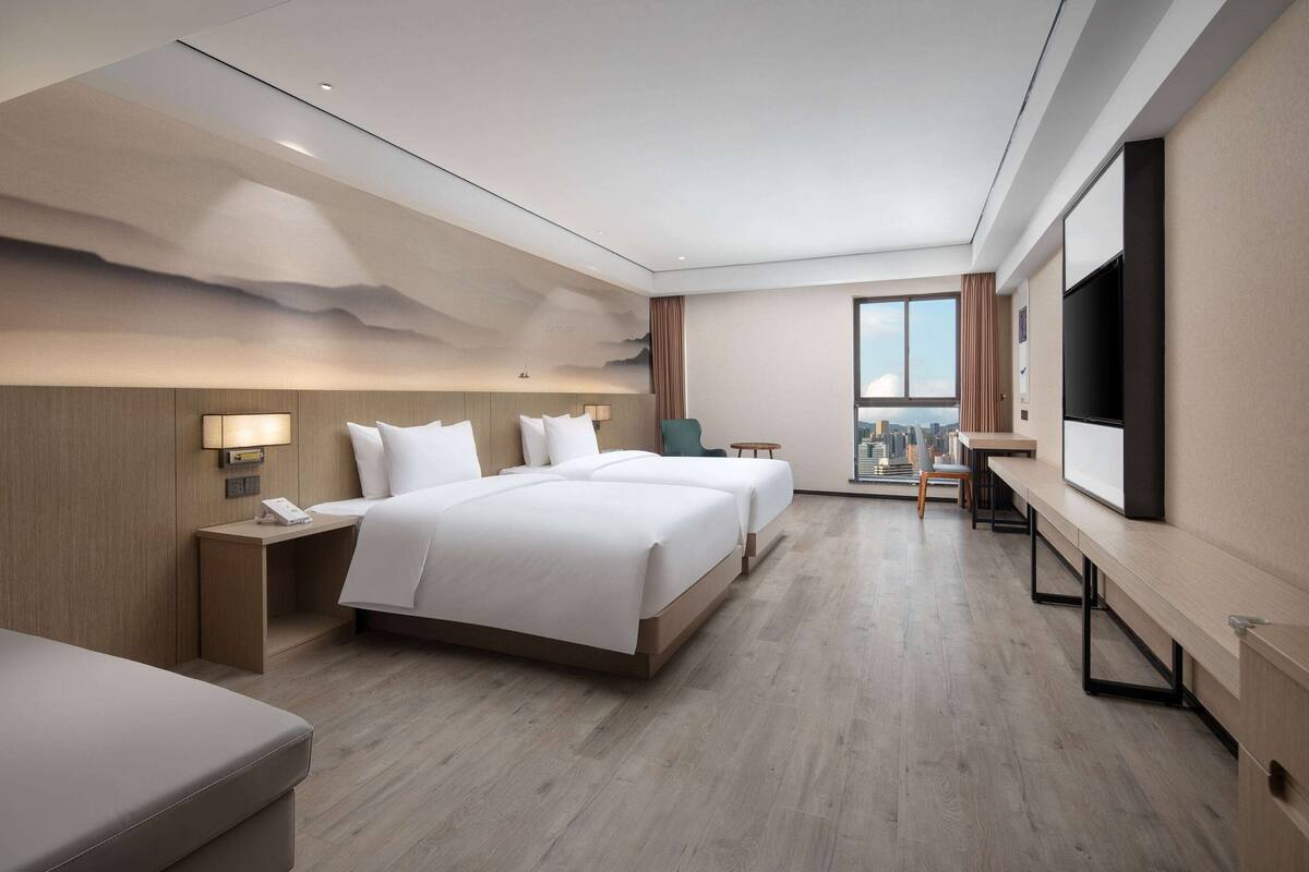Quarto de hotel moderno com uma cama grande, mesas de cabeceira, escrivaninha e televisão.