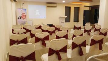 Sala de conferências com fileiras de cadeiras amarradas com fitas vermelhas, um pódio e uma tela de projeção exibindo um logotipo.