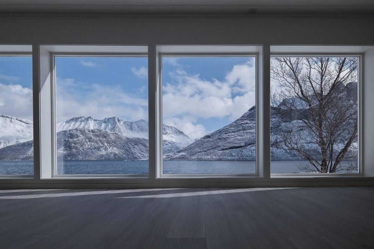 Quarto com uma grande janela que oferece vista para montanhas cobertas de neve e um lago.