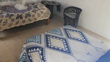 Quarto com telhado de colmo, duas camas com colchas estampadas, uma mesa pequena, uma cadeira e ar condicionado fixado na parede.