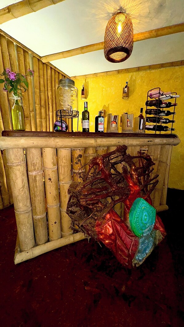Uma área de bar com fundo de bambu, diversos frascos e um lustre.