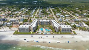 Vista aérea de um resort costeiro com vários edifícios altos, uma praia e uma piscina.