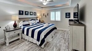 Quarto com cama, mesas de cabeceira, penteadeira, ventoinha no teto e obras de arte penduradas na parede.