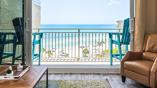 Varanda com vista para a praia, uma poltrona de couro e uma mesa de madeira com objetos decorativos.