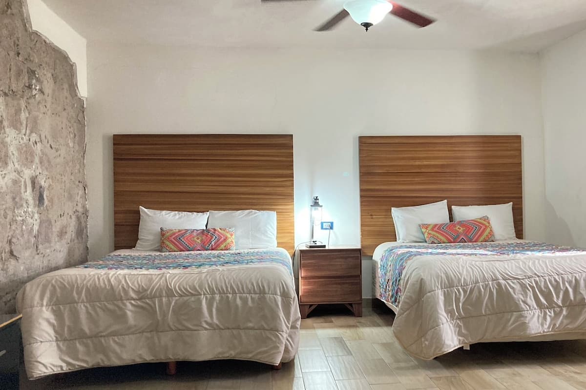 Quarto com duas camas, cabeceiras de madeira, mesa de cabeceira com abajur e ventoinha no teto.