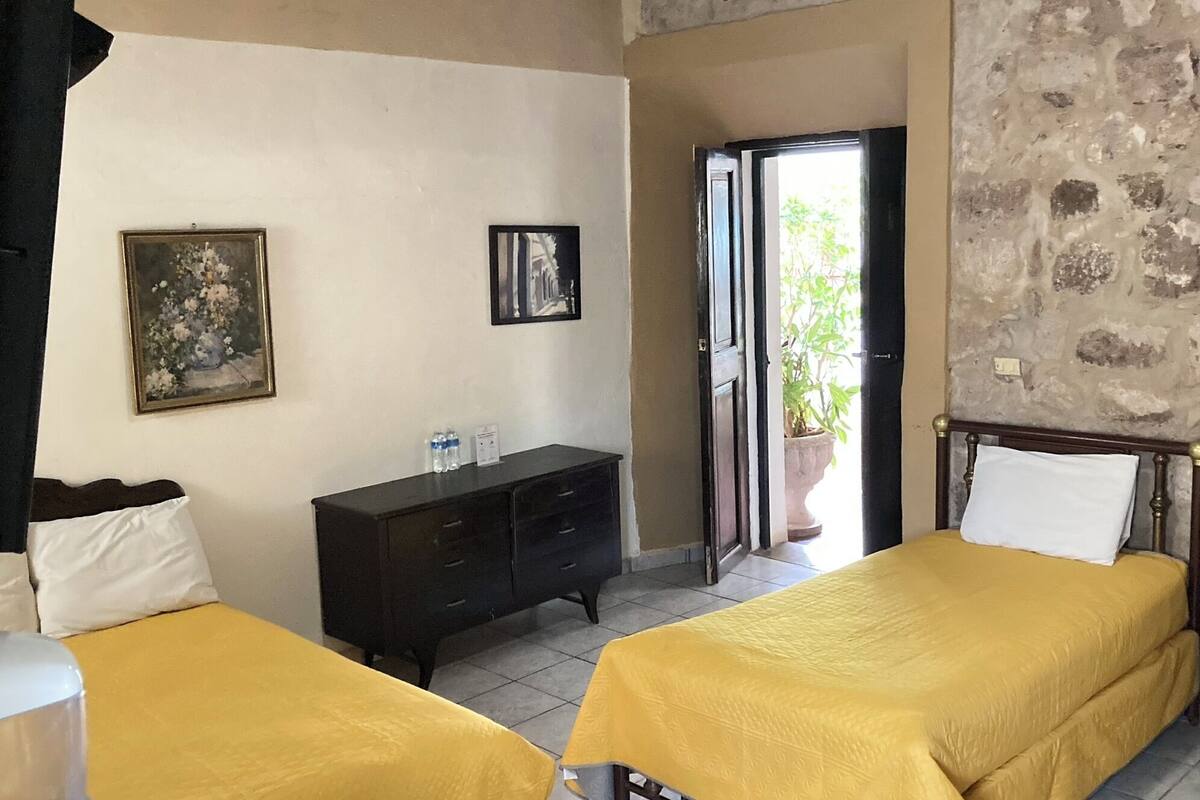 Quarto de hotel com duas camas, uma cômoda e porta para uma varanda.