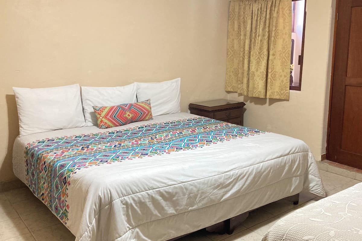 Uma cama com um edredom colorido, almofadas brancas e uma mesa de cabeceira de madeira com uma luminária.