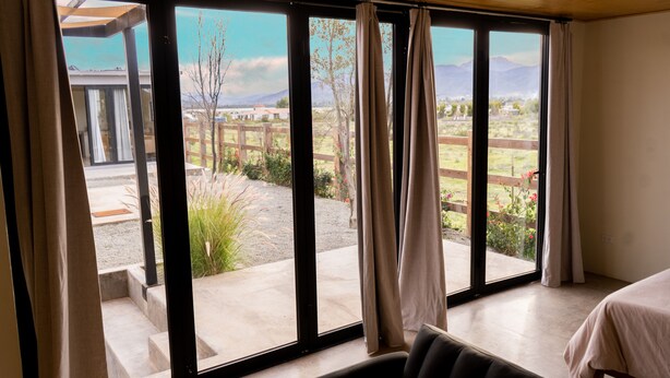 Quarto com amplas portas de vidro deslizantes que dão para um pátio com cerca de madeira, degraus e vista para uma paisagem montanhosa.