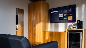 Quarto moderno com guarda-roupa de madeira, TV de tela plana exibindo serviços de streaming, máquina de café e mini-geladeira embutida.