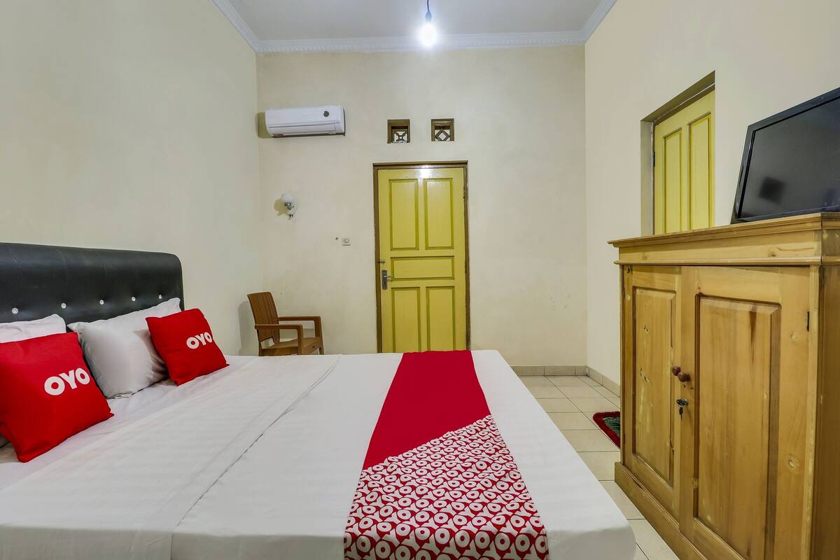 Quarto de hotel com cama, guarda-roupa de madeira, televisão e porta amarela.