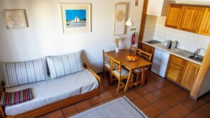 Espaço compacto com sofá, mesa de jantar, cadeiras e cozinha, incluindo pia e armários.