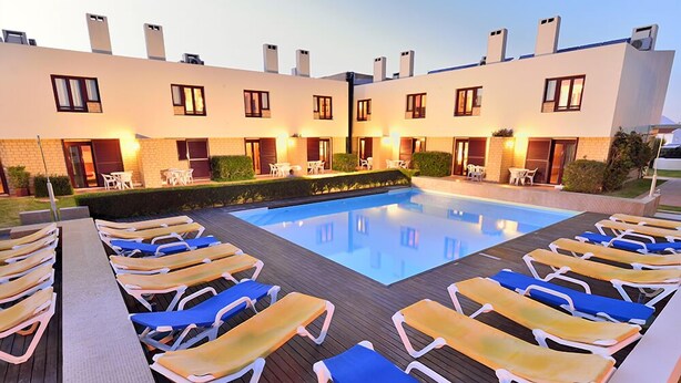 Um hotel moderno com piscina, rodeada por espreguiçadeiras.