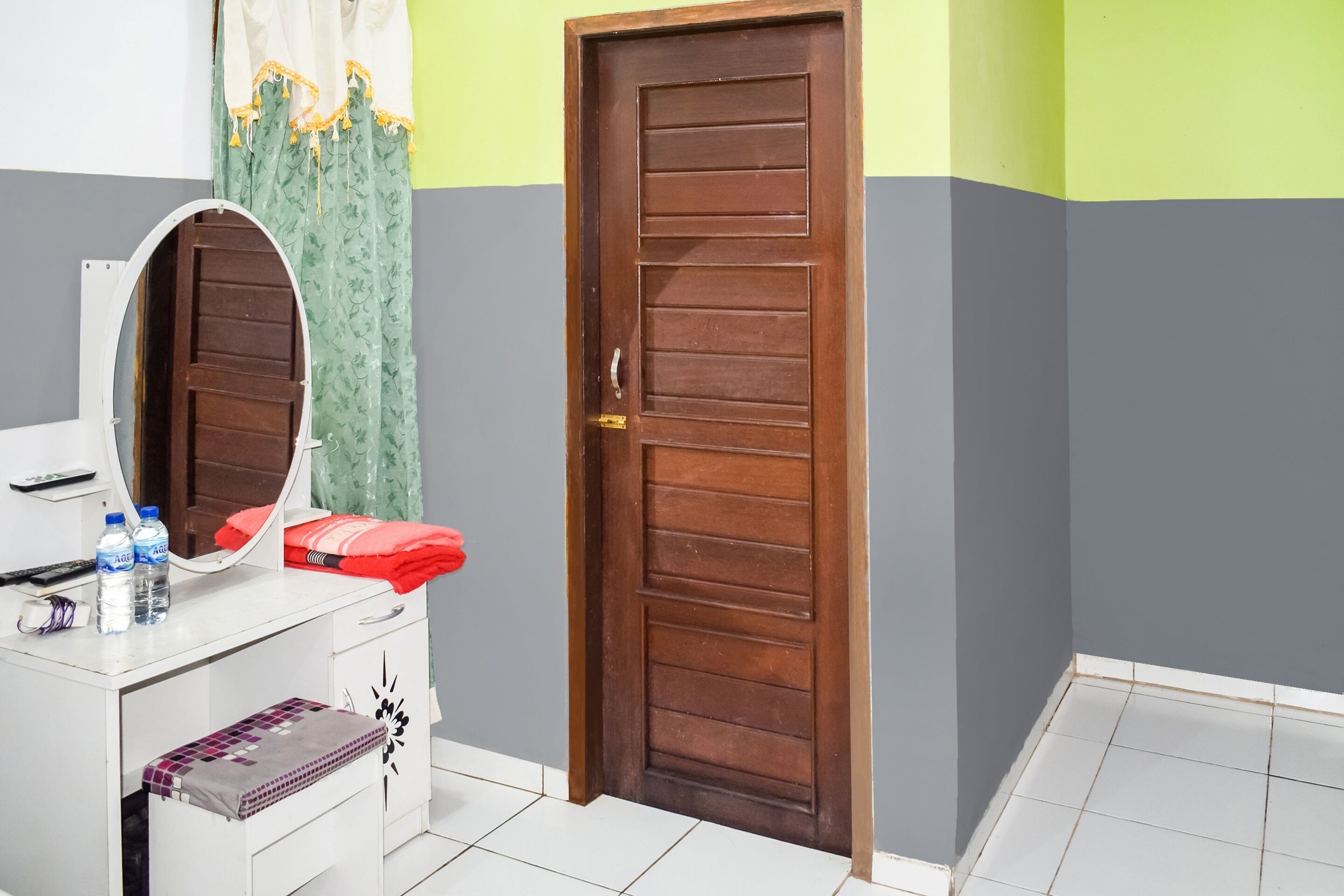 Um banheiro com porta de madeira, um espelho sobre um lavatório branco e parede verde e cinza.