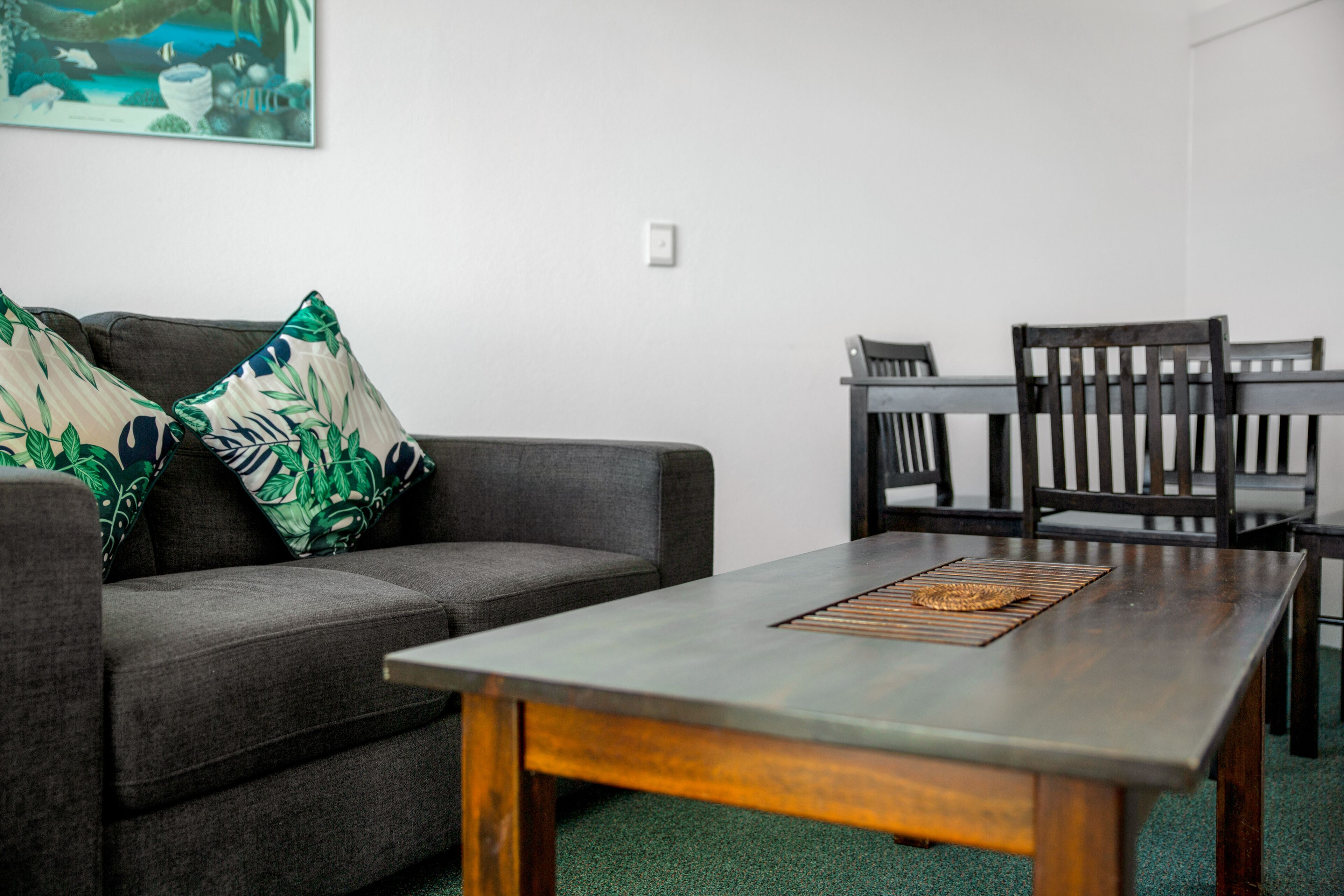Uma sala de estar com um sofá cinza, uma mesa de centro de madeira e uma mesa de jantar com cadeiras.