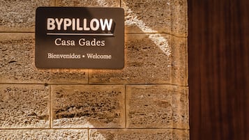 Uma placa com a inscrição "BYPILLOW Casa Gades", seguida de "Bienvenidos Welcome". Placa fixada em uma parede de pedra texturizada.