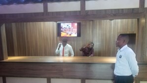Bancada de recepção com acabamento em madeira e uma televisão montada acima.
