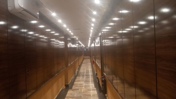Corredor com painéis de madeira, piso ladrilhado e iluminação embutida.