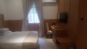 Quarto de hotel com cama, escrivaninha, cadeira, televisão e ar condicionado.