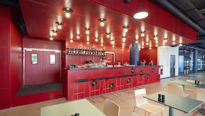 Uma área de bar moderna com detalhes em vermelho, diversas opções de assento e um balcão com vários tipos de bebidas.