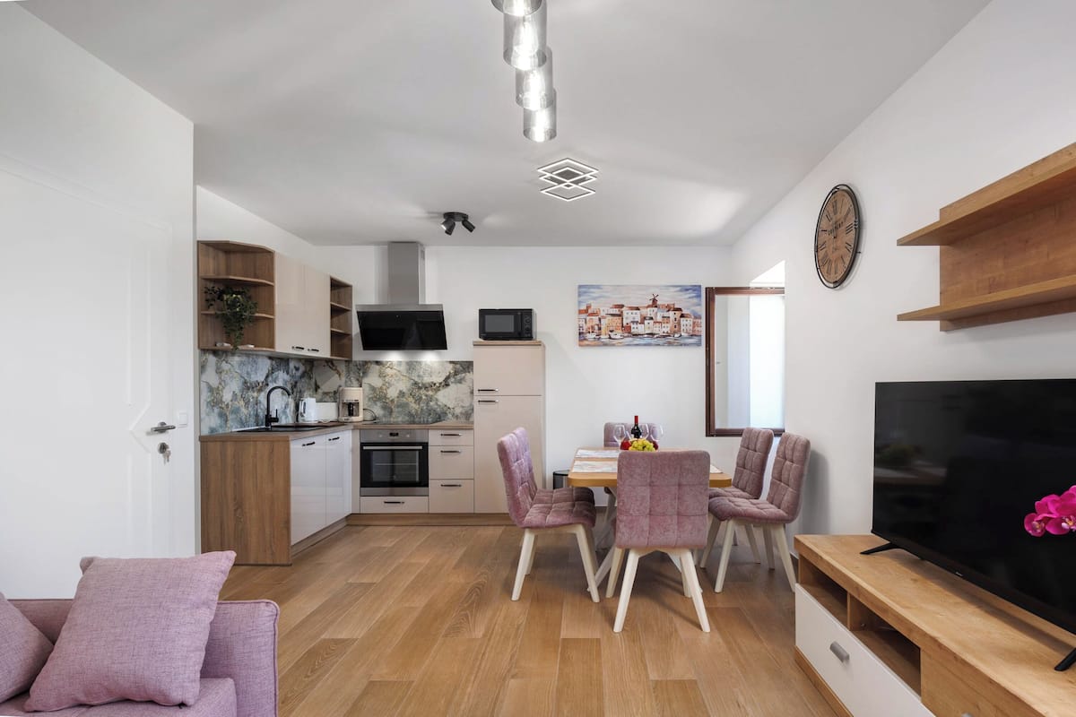 Cozinha moderna com armários de madeira, micro-ondas e área de jantar com cadeiras rosa e mesa de madeira.