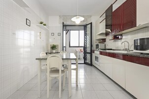 Uma cozinha moderna com armários brancos, bancada de granito e uma área de refeições com cadeiras brancas.