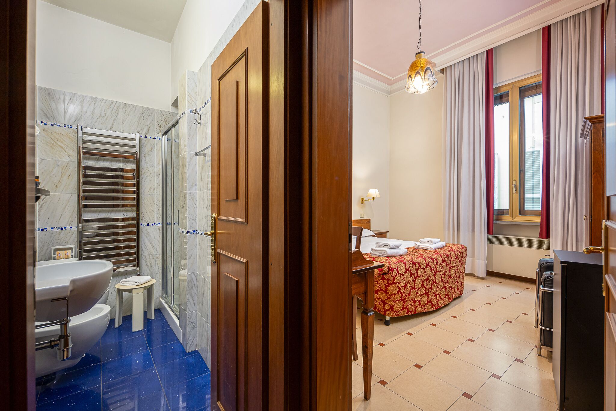 Quarto de hotel com banheiro, cama, escrivaninha e janela.