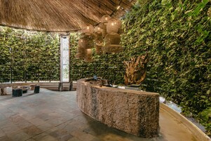 Uma área de recepção com balcão de pedra, luminárias pendentes esféricas e uma parede coberta por vegetação.