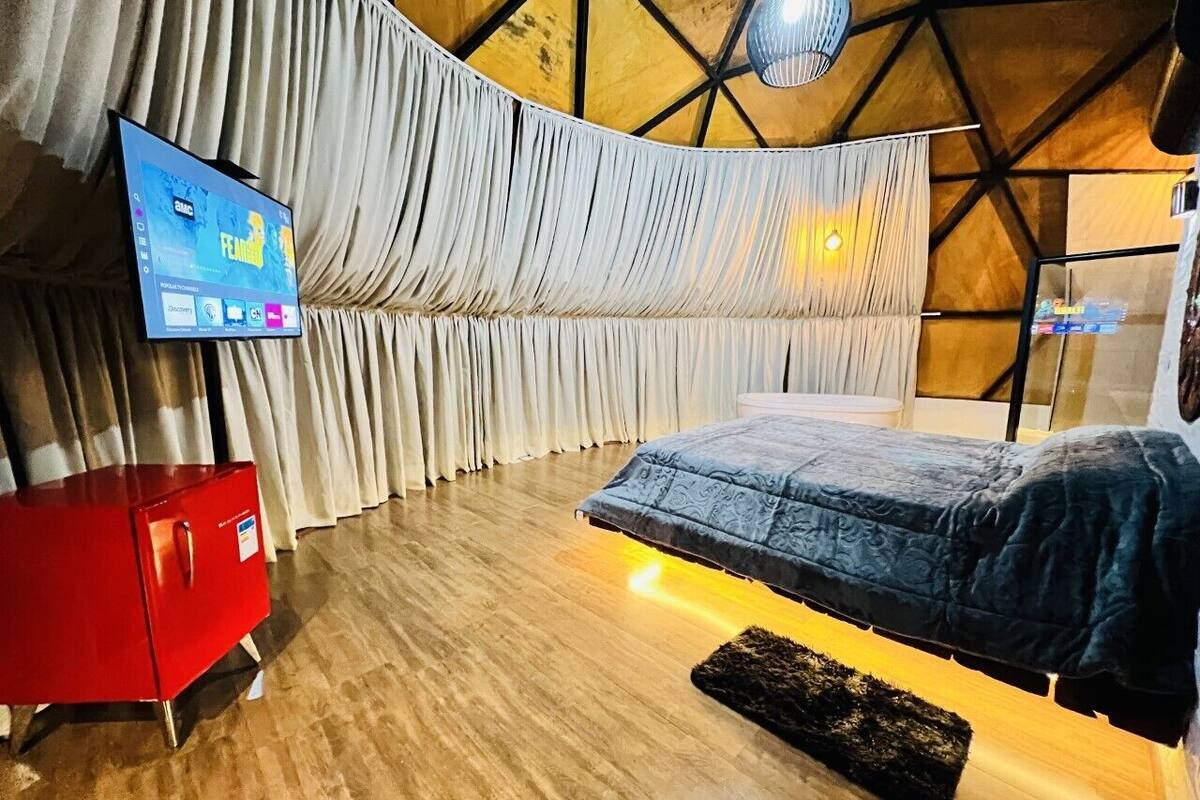 Quarto com teto curvo, cama, armário vermelho e televisão na parede.
