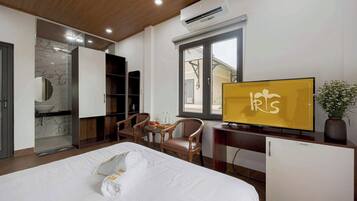 Quarto de hotel com cama, escrivaninha, cadeira, guarda-roupa e televisão.