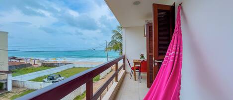 Varanda com vista para a praia, mesa com cadeiras e uma rede rosa.