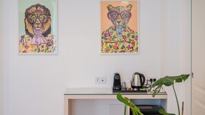 Duas obras de arte emolduradas em uma parede acima de uma mesa com uma cafeteira e uma planta.