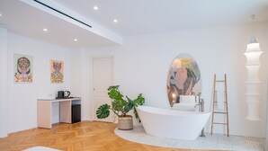 Um banheiro moderno com uma banheira livre, uma pia e um espelho. Há uma escada de madeira encostada na parede e um vaso de planta no chão.