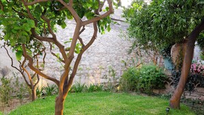 Um jardim com muro de pedra, diversas plantas e uma árvore com escultura de metal na grama.