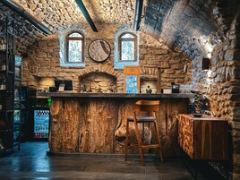 Um espaço de bar rústico com paredes de pedra, balcão de madeira e um relógio grande na parede.