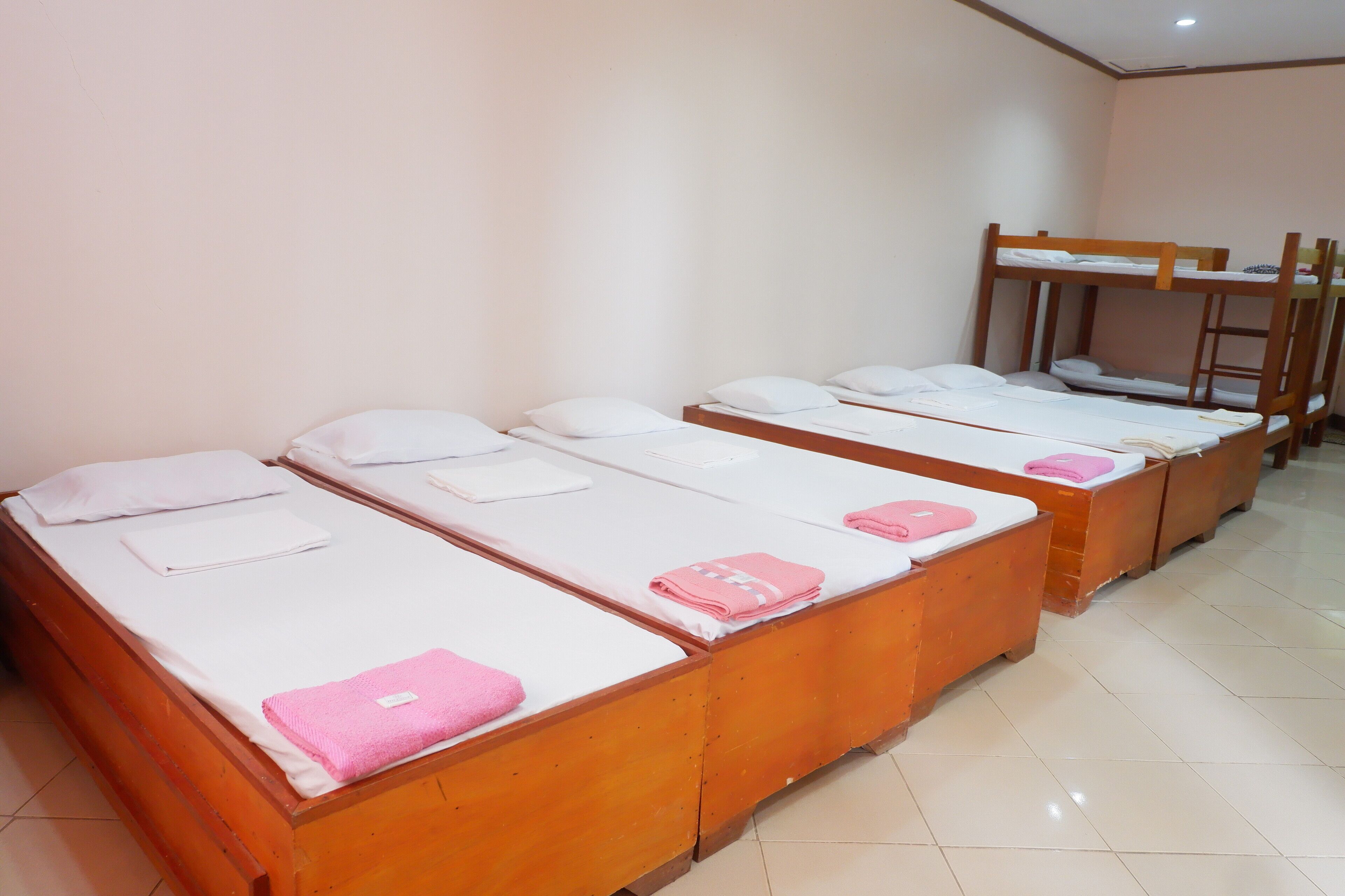 Uma fileira de beliches de madeira com roupa de cama branca e toalhas cor de rosa.