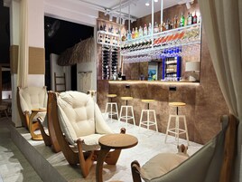 Uma área de bar com assentos acolchoados, balcão com diversos tipos de bebidas e banquetas.