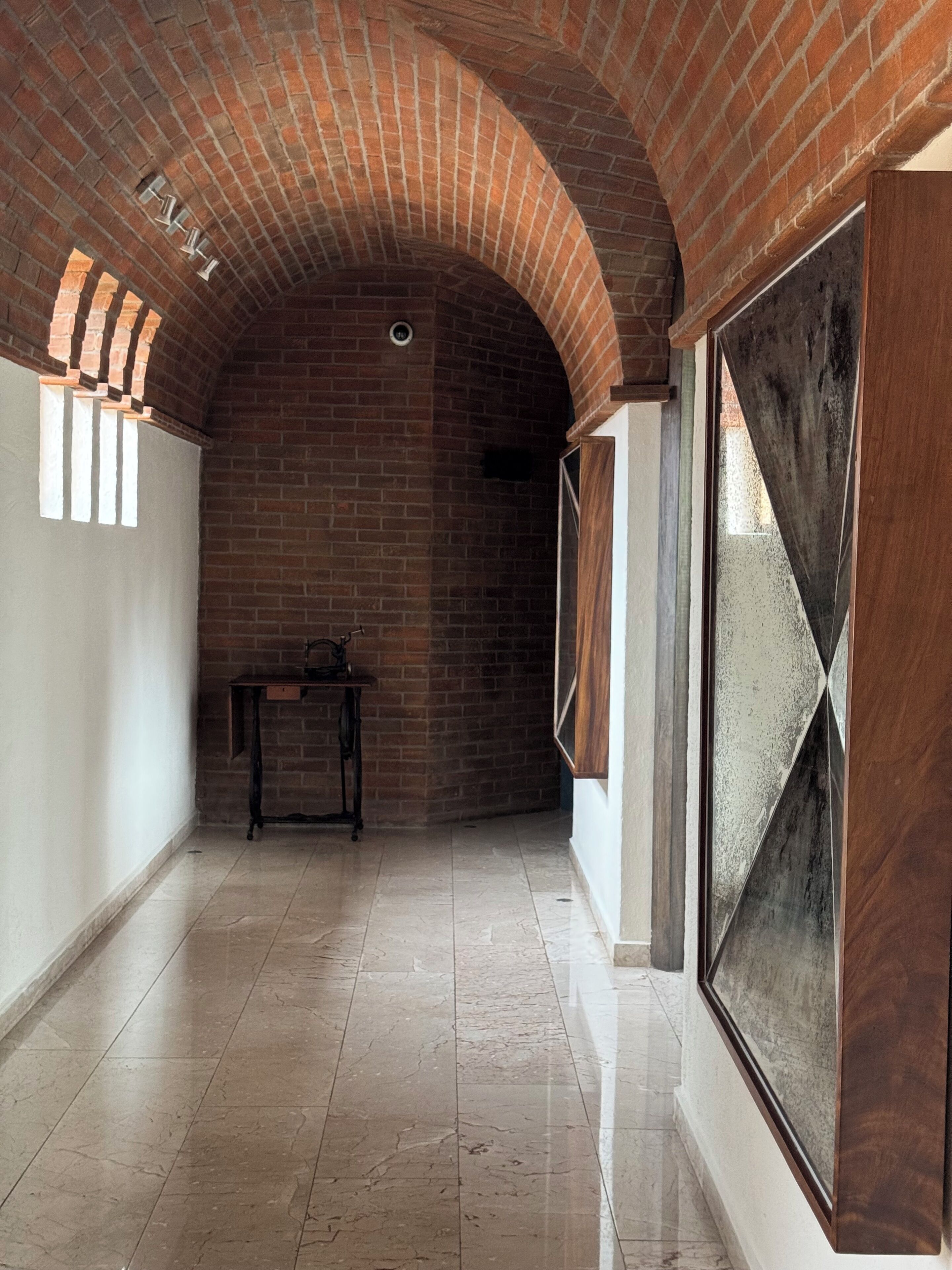 Um interior com teto de tijolos, piso de azulejos e uma grande janela com padrão geométrico.