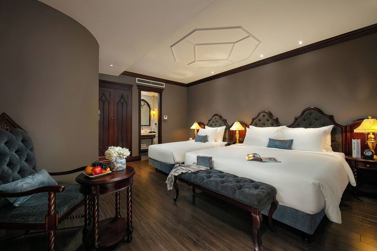 Quarto de hotel com duas camas, área de estar e mesa de jantar.